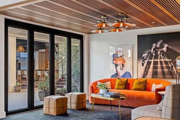 Uma sala de estar moderna com um sofá grande laranja, uma mesa de centro redonda e vista para a área externa através de grandes portas de vidro deslizantes.