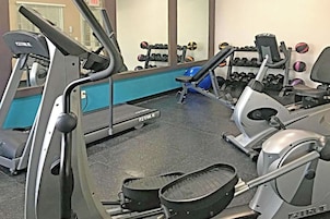 Uma academia com diversos equipamentos de exercício, incluindo esteiras, bicicleta ergométrica e pesos livres.