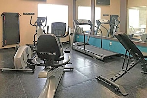 Academia com diversos equipamentos de exercício, incluindo bicicleta ergométrica, elíptico, esteira e banco de musculação.