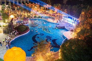 Área de piscina com uma fonte, cercada por árvores e uma galeria coberta.