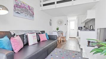 Um apartamento moderno com um sofá cinzento, almofadas coloridas, um tapete com bolinhas, área de refeições e cozinha compacta.