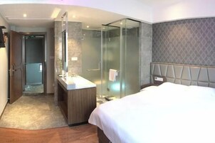 Quarto de hotel moderno com uma cama grande, chuveiro em cabine de vidro, toucador com espelho e parede com padrão.
