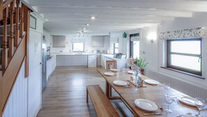 Uma cozinha ampla com uma ilha central, piso de madeira e uma área de refeições preparada para seis pessoas, incluindo um banco.