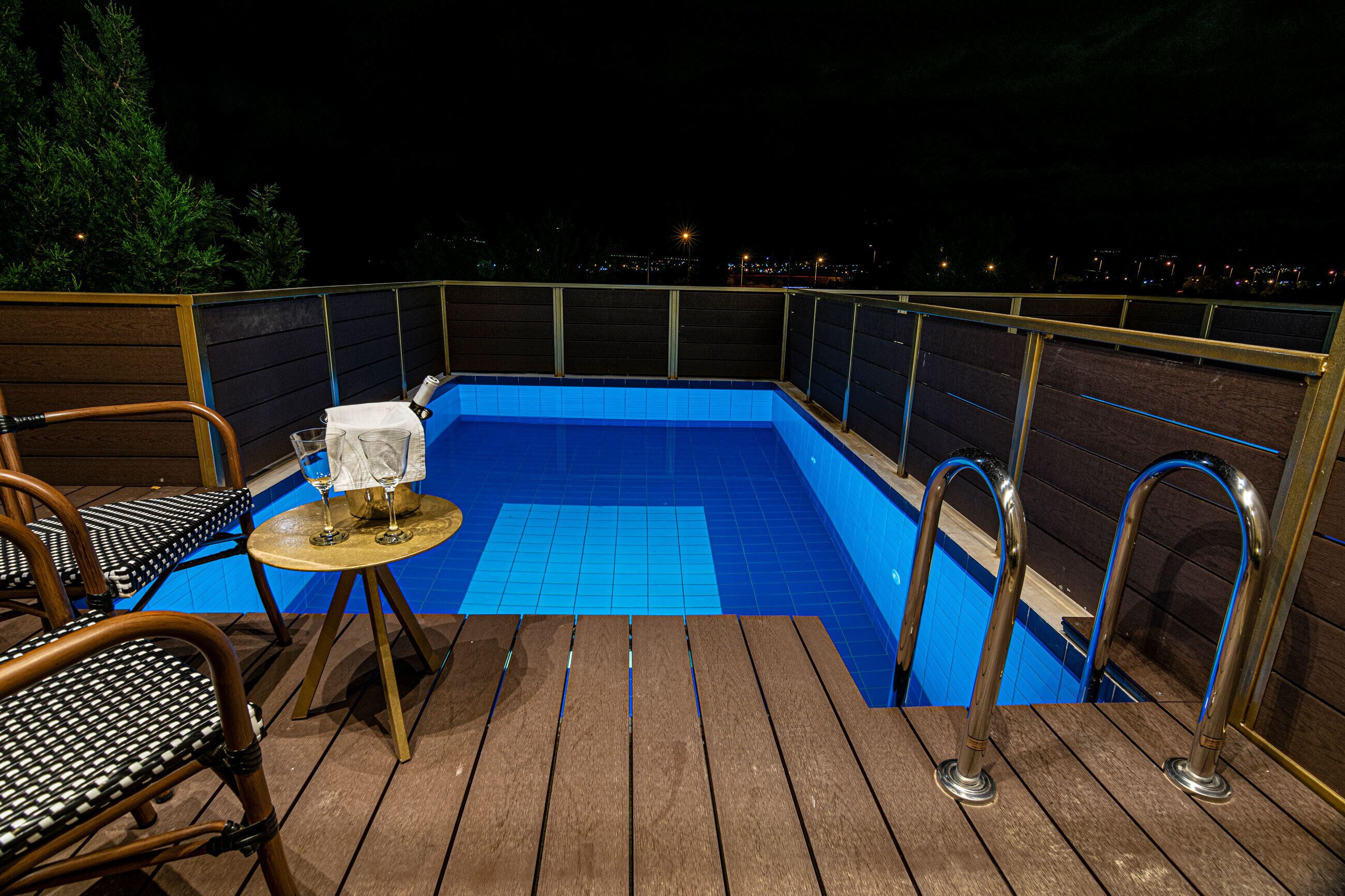 Um deck de madeira com piscina, grades de metal e duas cadeiras de vime.