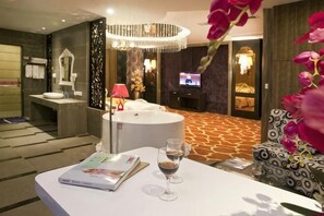 Um saguão de hotel com uma área de estar circular, uma mesa de recepção, uma televisão e uma planta decorativa.