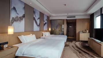 Quarto de hotel com duas camas, uma escrivaninha, televisão e obras de arte nas paredes.