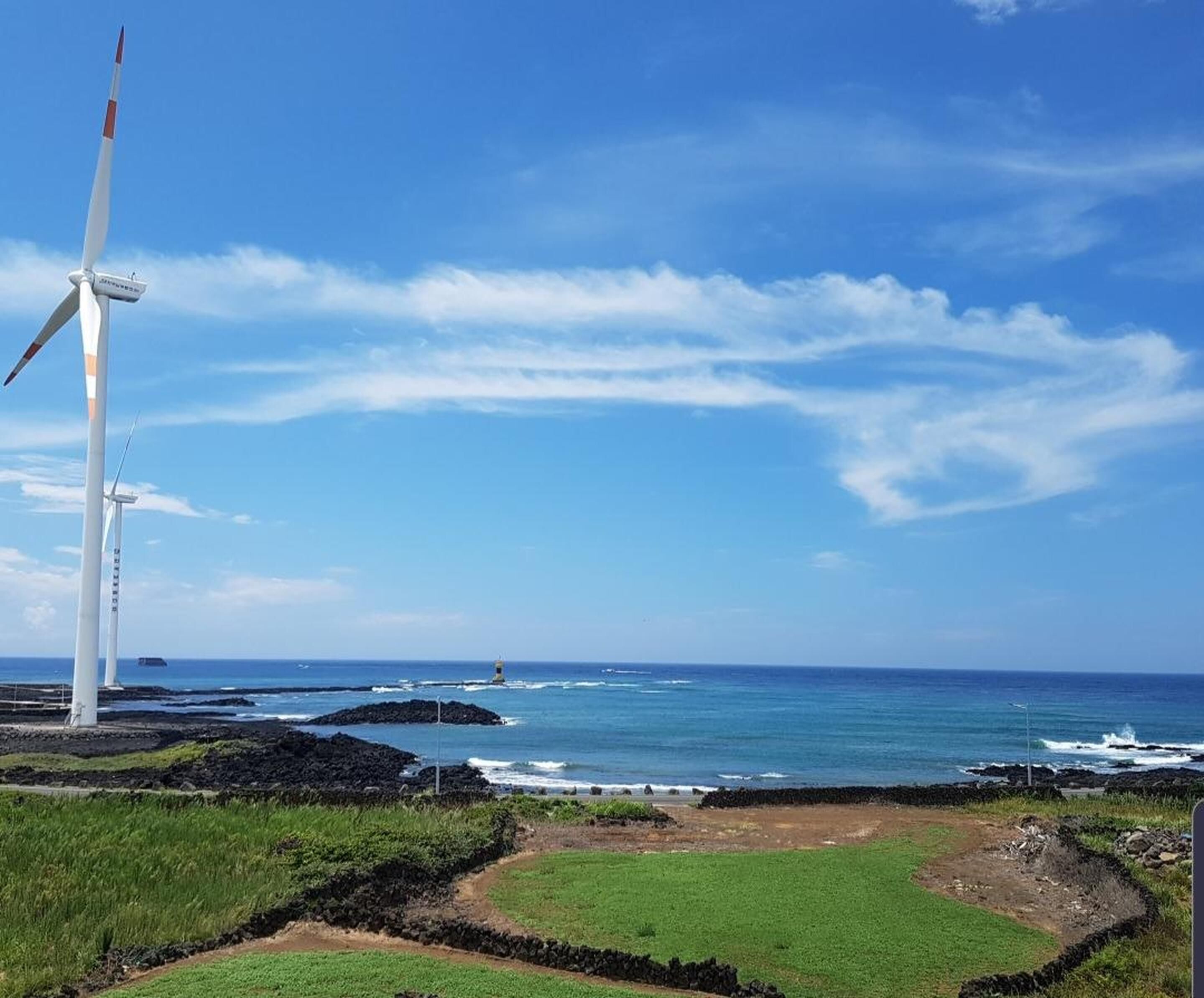 Paisagem costeira com uma turbina eólica grande e vista clara do oceano.