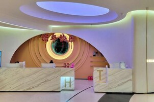 Uma área de recepção de hotel moderna, com balcões de mármore identificados pelas letras 'H' e 'T', uma parede decorativa circular e um design de teto rebaixado.