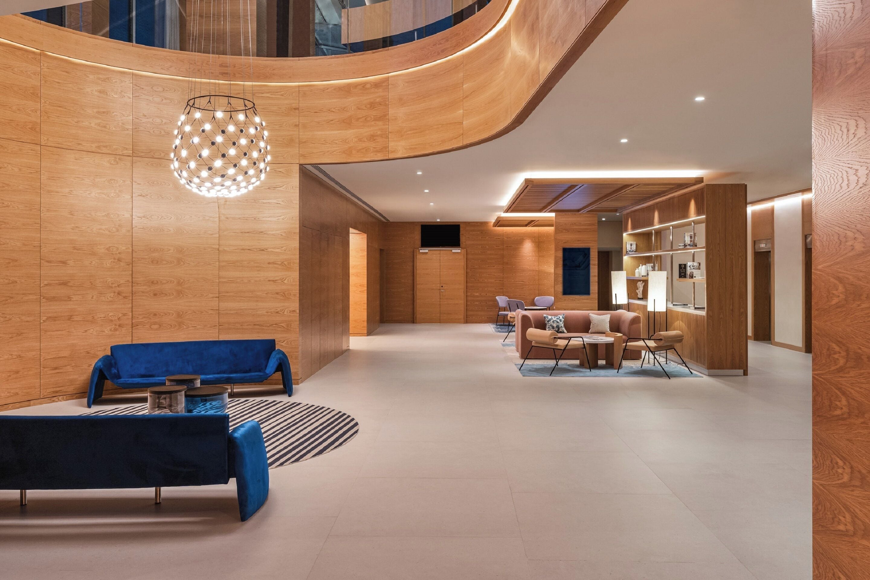 Um hall moderno com uma parede curva de madeira, um sofá azul, uma mesa redonda e uma área de estar com uma mesinha de centro.