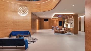 Um hall moderno com uma parede curva de madeira, um sofá azul, uma mesa redonda e uma área de estar com uma mesinha de centro.