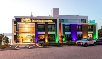 Um hotel boutique moderno com um letreiro chamativo, grandes janelas e um estacionamento com carros.