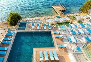 Uma área de piscina com várias espreguiçadeiras e um deque de madeira com vista para o mar.