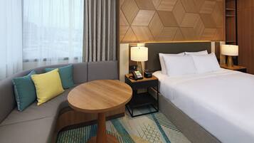 Quarto de hotel com cama, sofá, mesa redonda, mesa de cabeceira com luminárias e cabeceira com padrão geométrico.