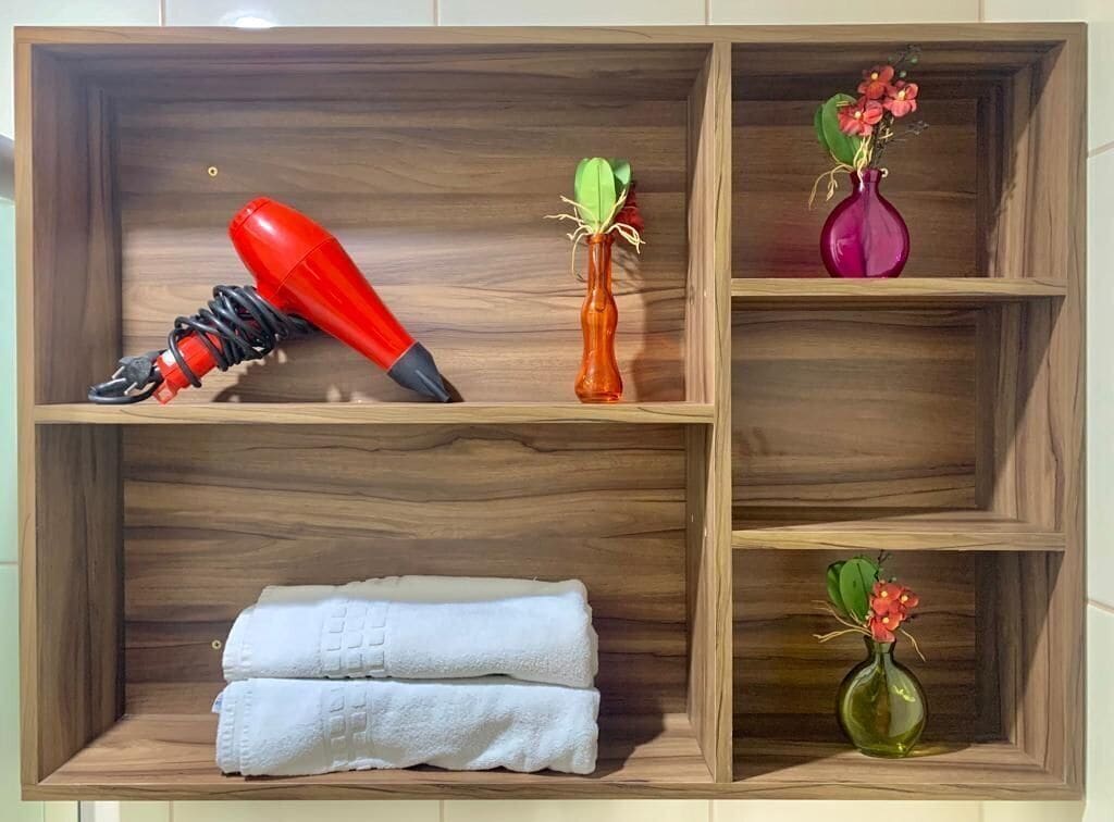 Uma prateleira de madeira com toalhas, um secador de cabelo vermelho e dois vasos com flores.