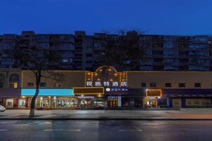 Um hotel com entrada destacada, diversas lojas no térreo e estacionamento.