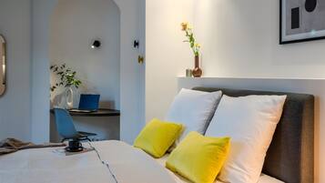 Quarto moderno com cama, escrivaninha com laptop, cadeira e vaso com flores fixado na parede.