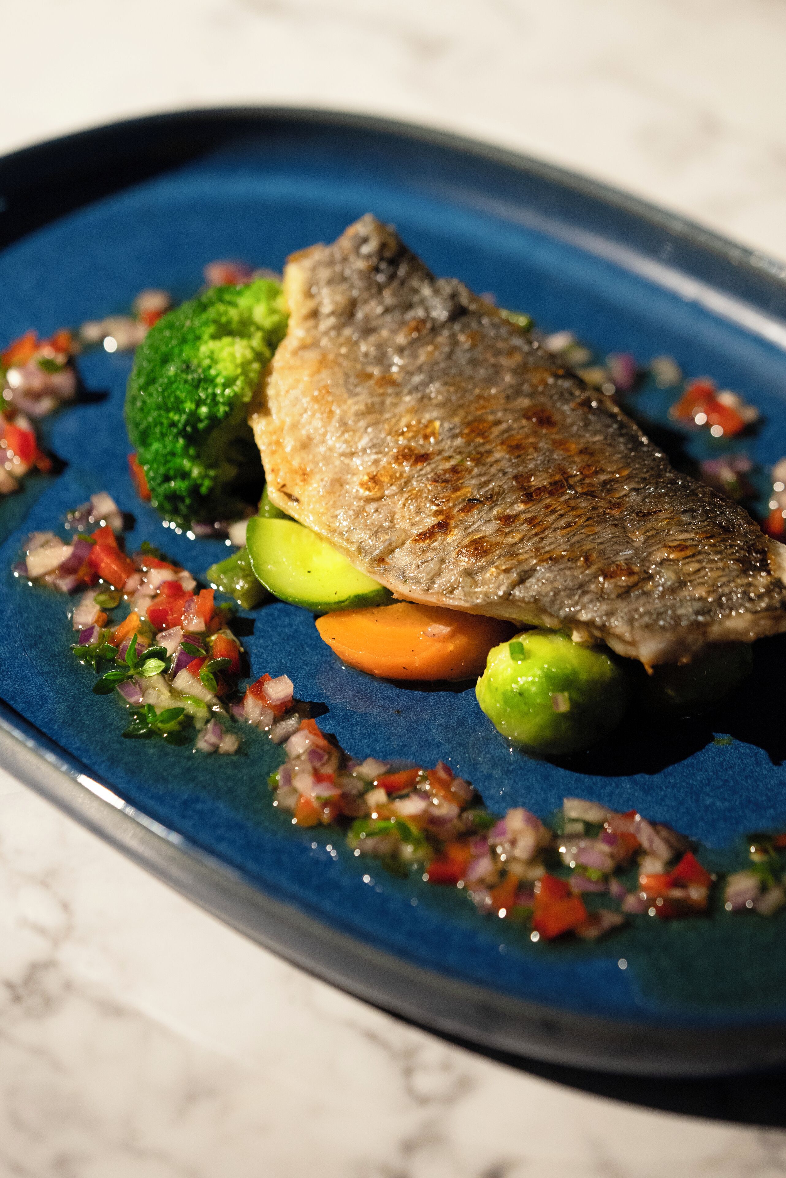 Um prato com peixe grelhado, brócolis, cenoura e um molho.
