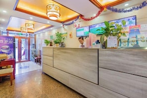 Área de recepção de hotel com balcão de madeira, tela digital e uma planta.