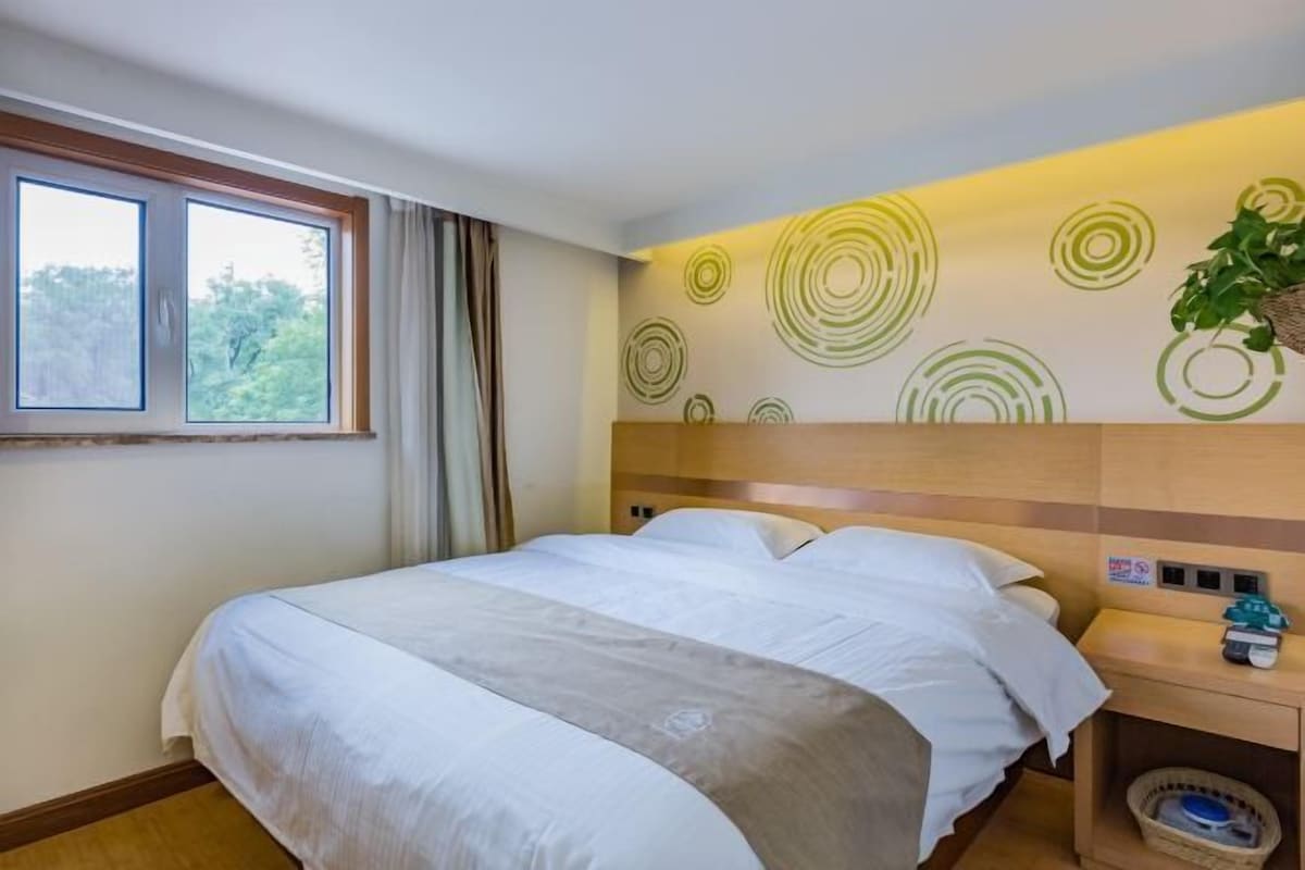 Quarto de hotel com cama, janela com cortinas, parede com desenhos circulares e mesa de cabeceira com cesta.