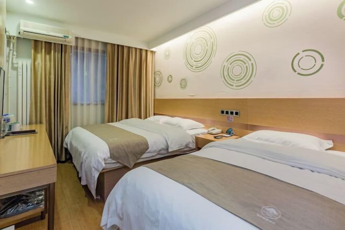 Quarto de hotel com duas camas, uma escrivaninha de madeira, um telefone e uma parede com padrões circulares.