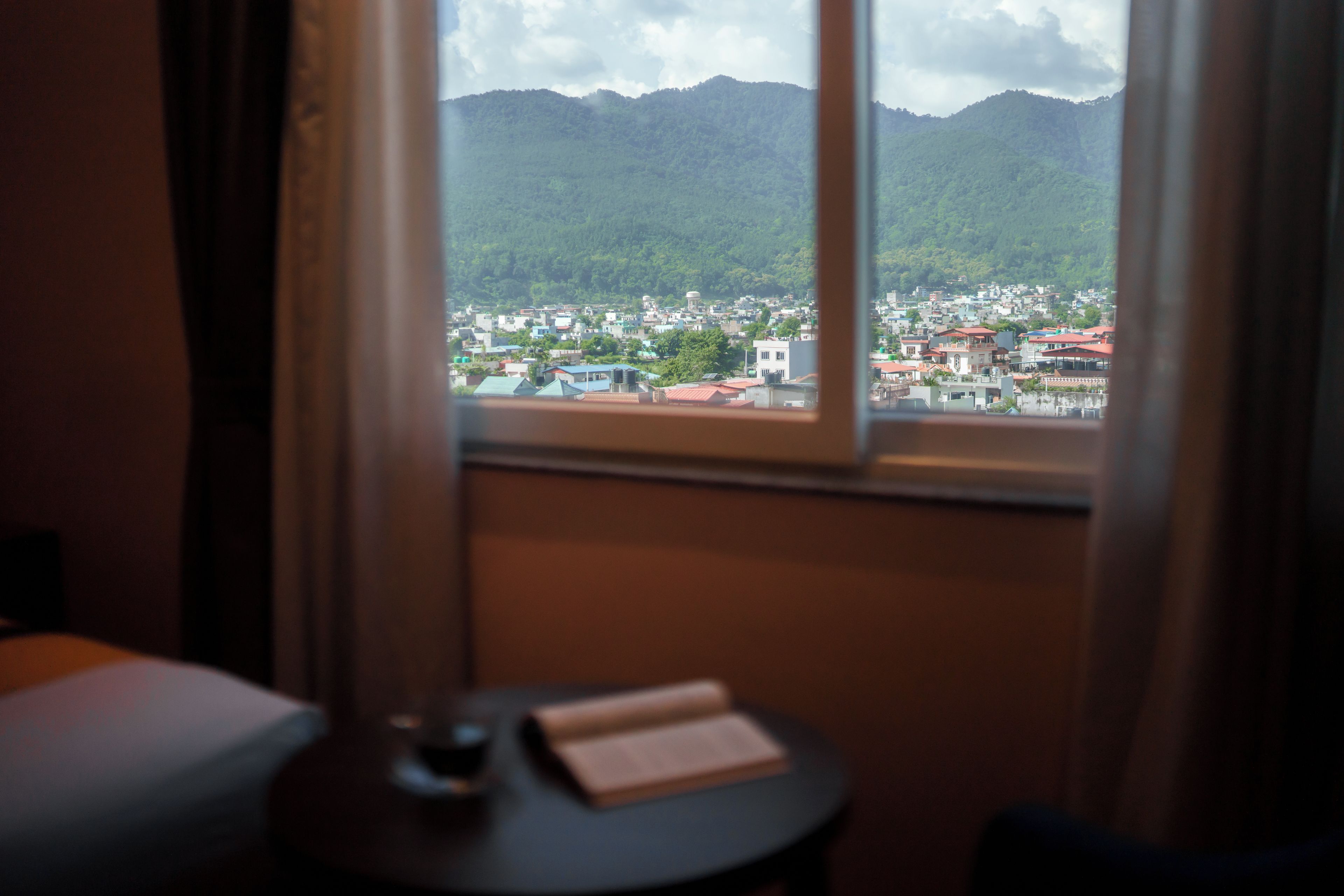 Quarto com janela vista para uma cidade e montanhas.