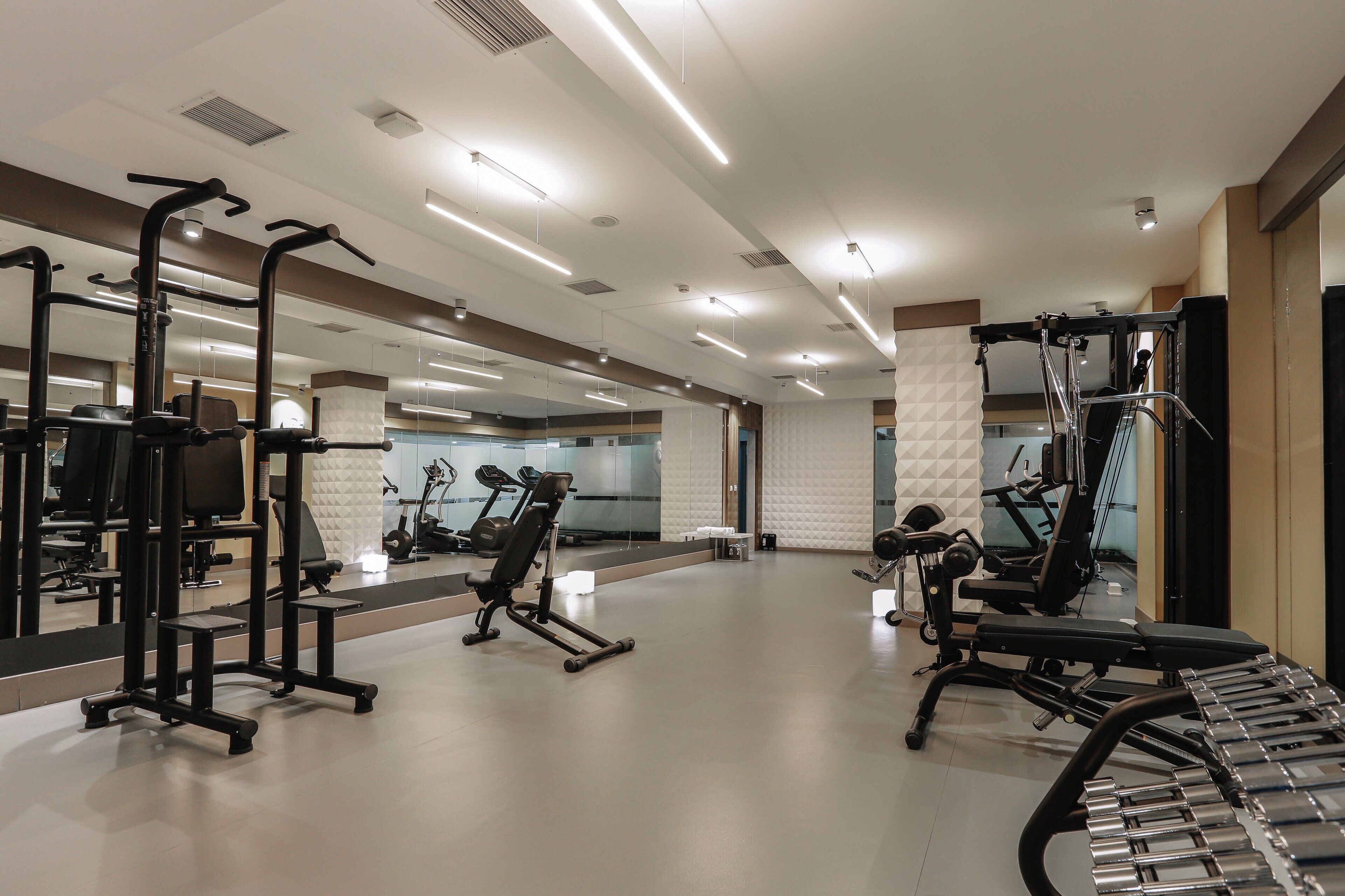 Uma academia moderna com diversos equipamentos de exercício, um espelho grande e um espaço amplo e bem cuidado.