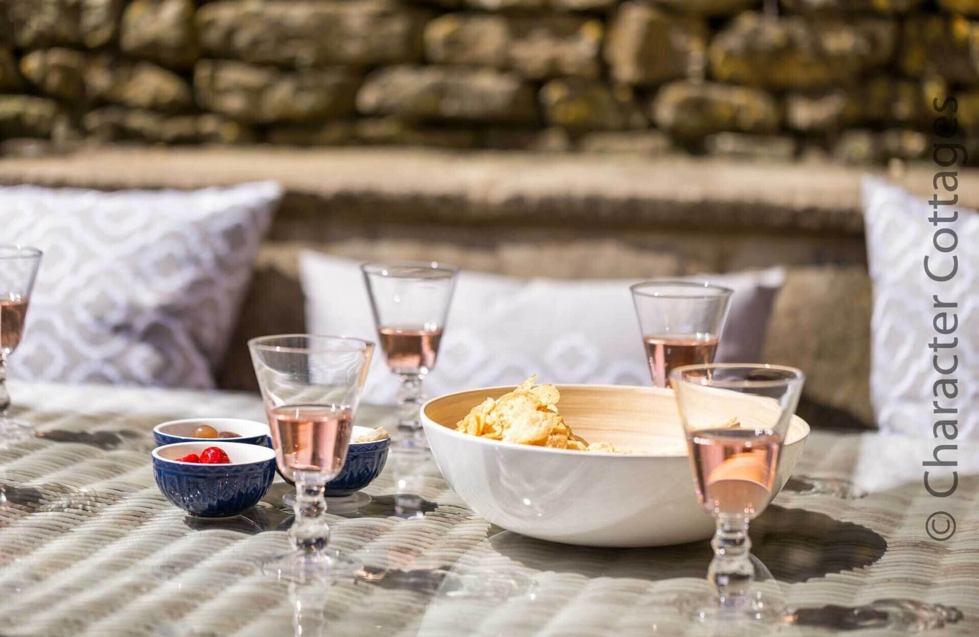 Uma mesa com um prato de comida, copos de uma bebida rosa e uma pequena tigela com um item vermelho.