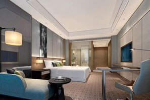 Quarto de hotel moderno com uma cama, um sofá, uma mesinha e uma televisão.
