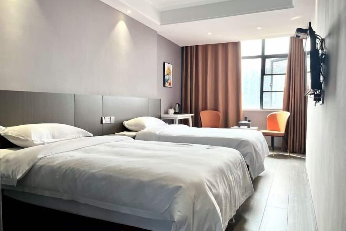 Quarto de hotel com duas camas, uma escrivaninha, uma cadeira e uma janela com cortinas.