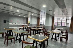 Uma área de refeições com várias mesas e cadeiras, parede de mármore e uma janela com cortinas.