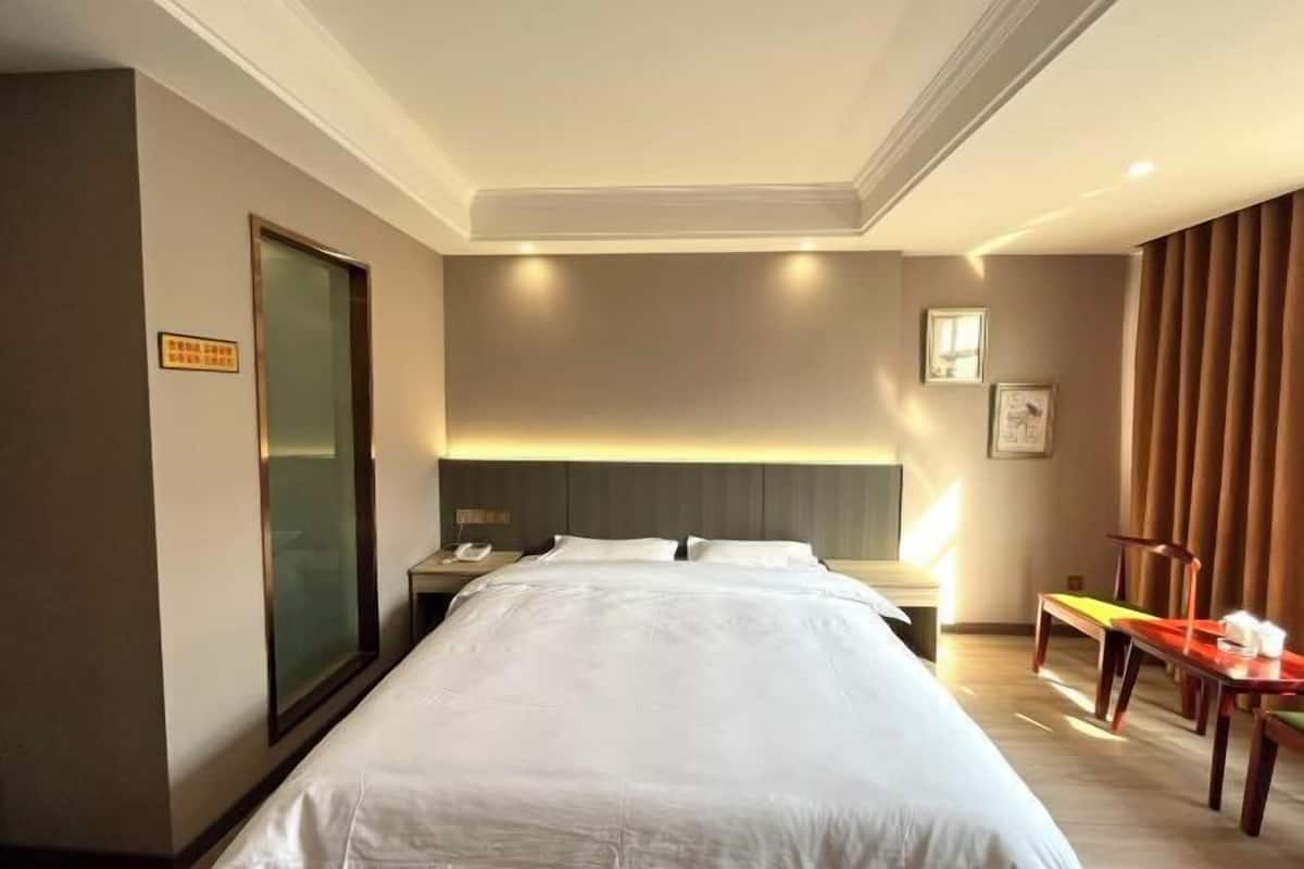 Quarto de hotel com uma cama grande, mesas de cabeceira, uma escrivaninha e uma cadeira.