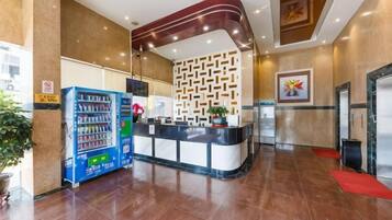 Área de recepção de hotel com máquina de venda automática, balcão de atendimento e parede com padrão geométrico.