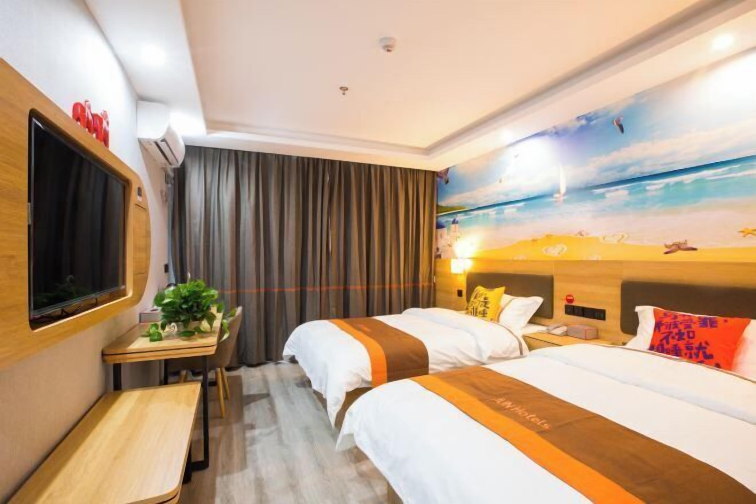 Quarto de hotel com duas camas, uma escrivaninha, uma televisão e um mural com uma cena de praia.