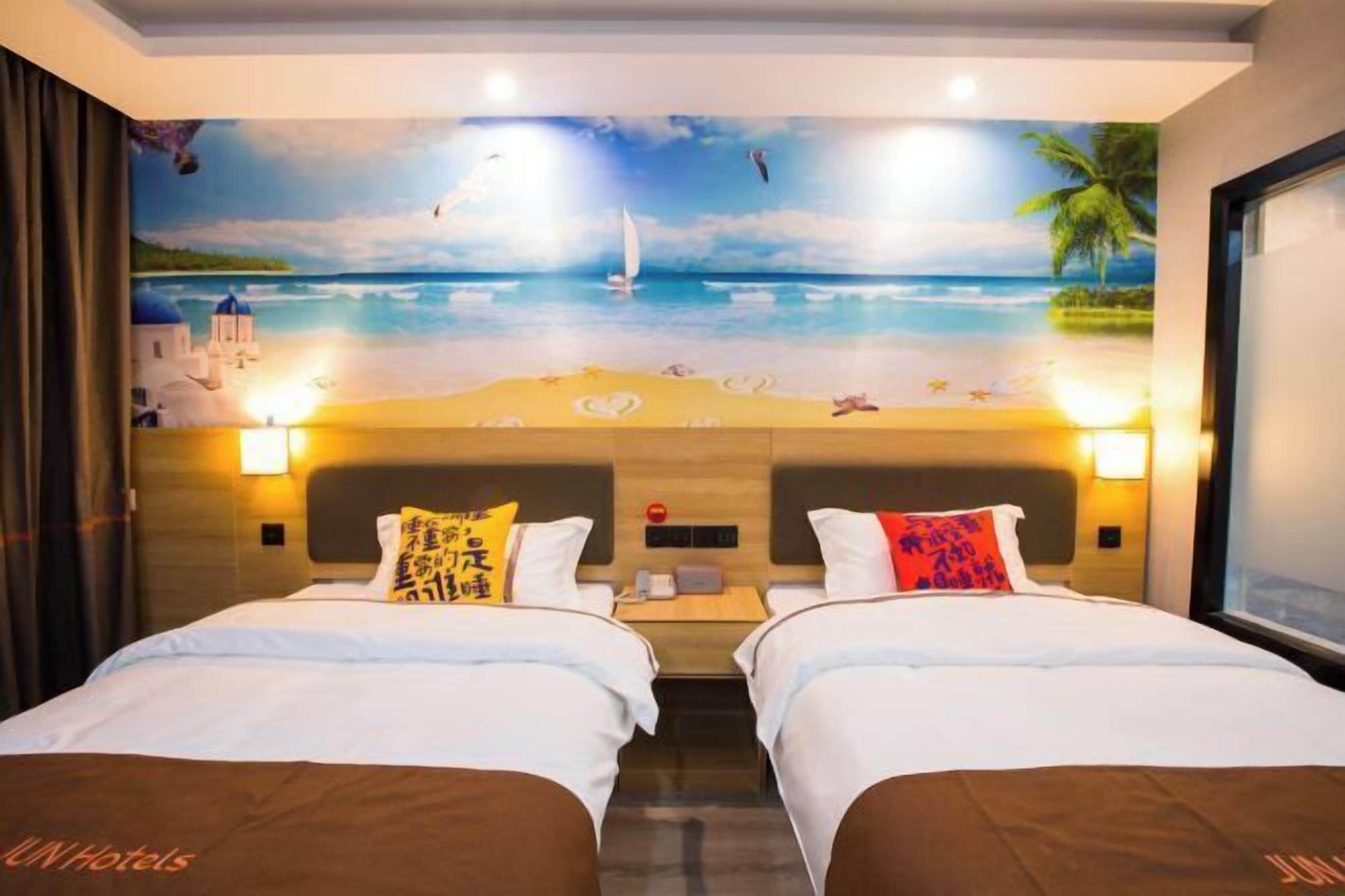 Quarto de hotel com duas camas, um mural com uma cena de praia e uma mesa de cabeceira com abajur.