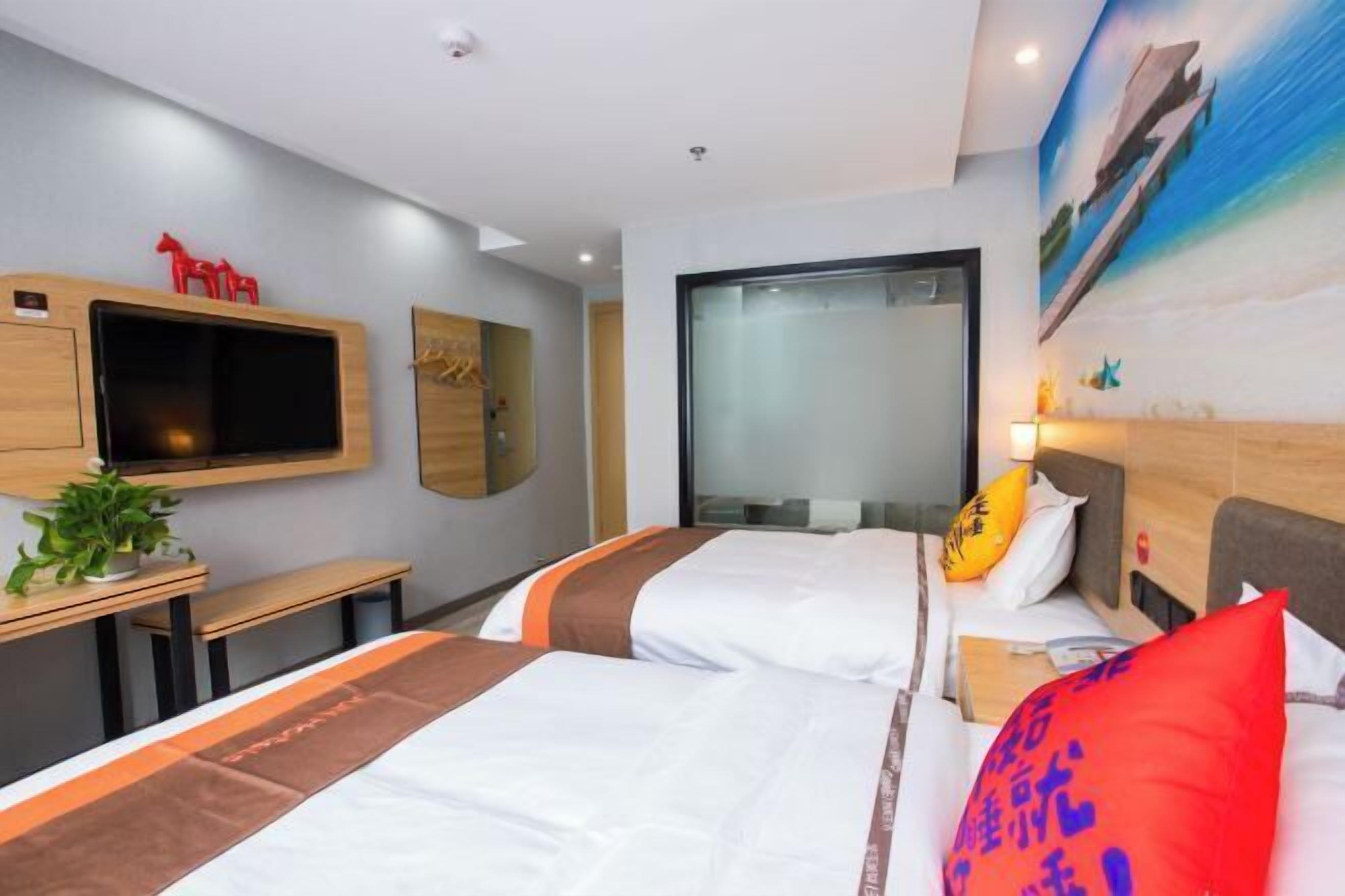 Quarto de hotel com duas camas, televisão, secretária com planta e uma janela grande.