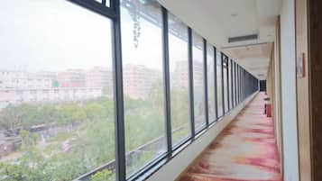 Um corredor com amplas janelas, tapete vermelho e vista para edifícios e áreas verdes lá fora.