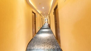 Corredor de hotel com piso estampado, portas em ambos os lados e uma luminária no teto.