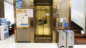 Um elevador com porta de vidro, uma lixeira e um contentor de reciclagem.