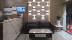 Uma área de recepção com design moderno, destacando-se por um balcão de mármore, um sofá de couro preto e uma pequena mesa.