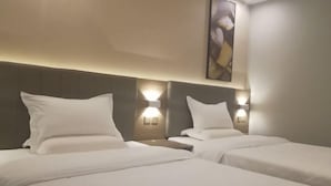 Quarto de hotel com duas camas, cada uma com roupa de cama branca e cabeceiras, e luminárias de cabeceira.