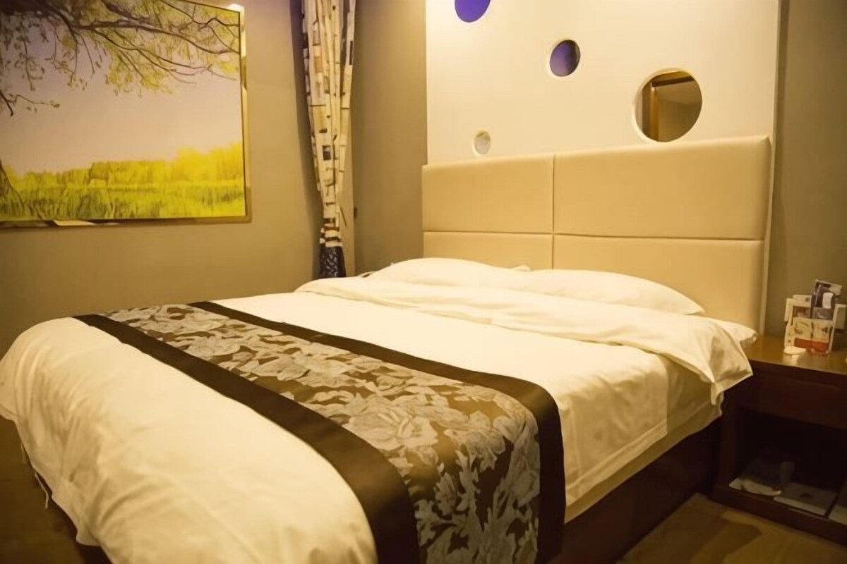 Quarto de hotel com cama, cabeceira com recortes circulares, mesa de cabeceira e pintura pendurada na parede.