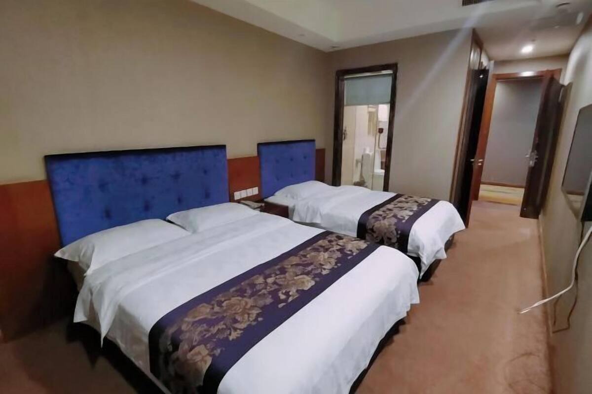 Quarto de hotel com duas camas, cada uma com cabeceira azul e roupa de cama branca.
