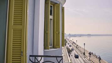 Um edifício costeiro com persianas verdes, varanda e vista para um mar calmo e um calçadão.