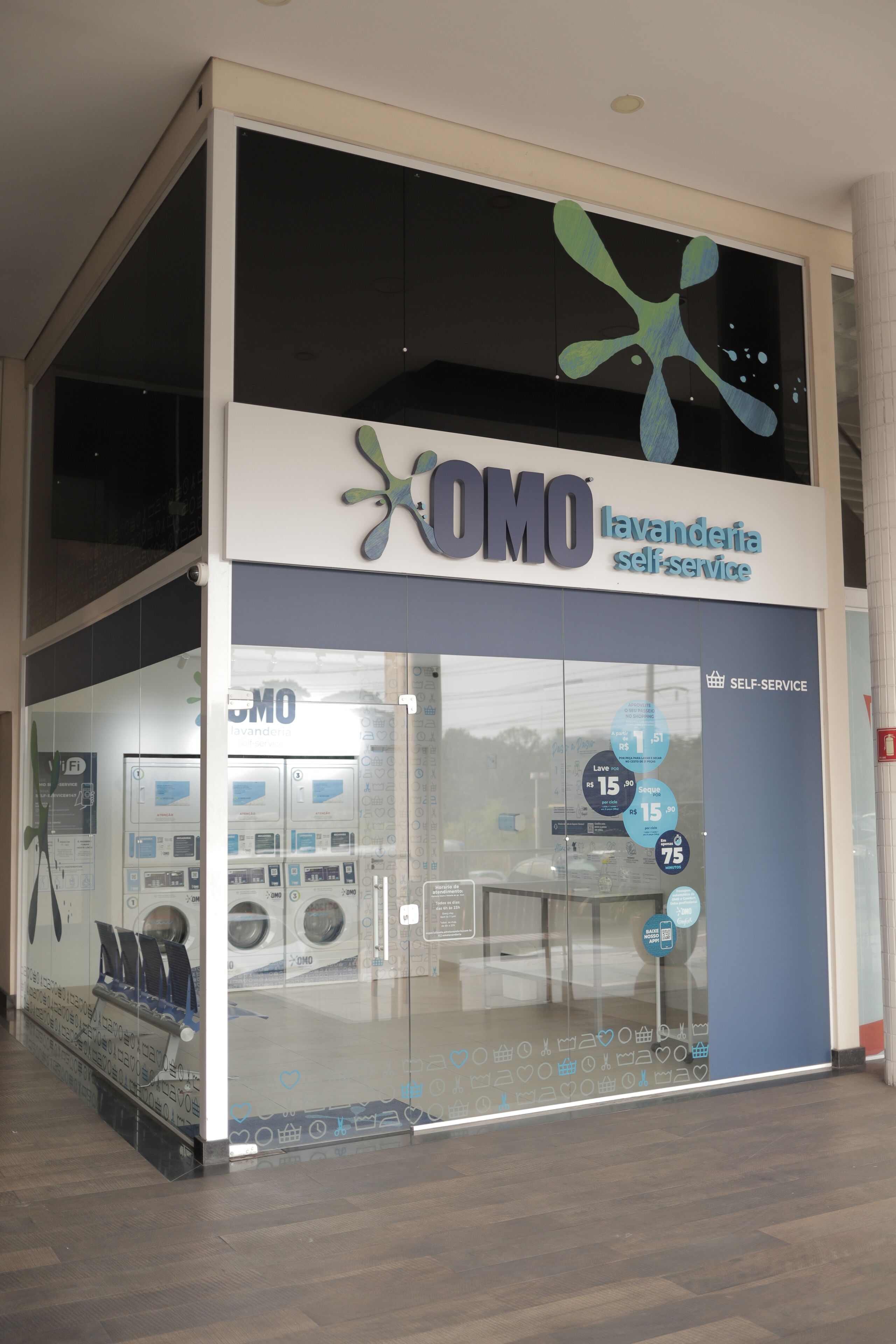 Uma lavanderia automática com paredes de vidro, um logotipo e uma placa indicando diversas opções de serviço.