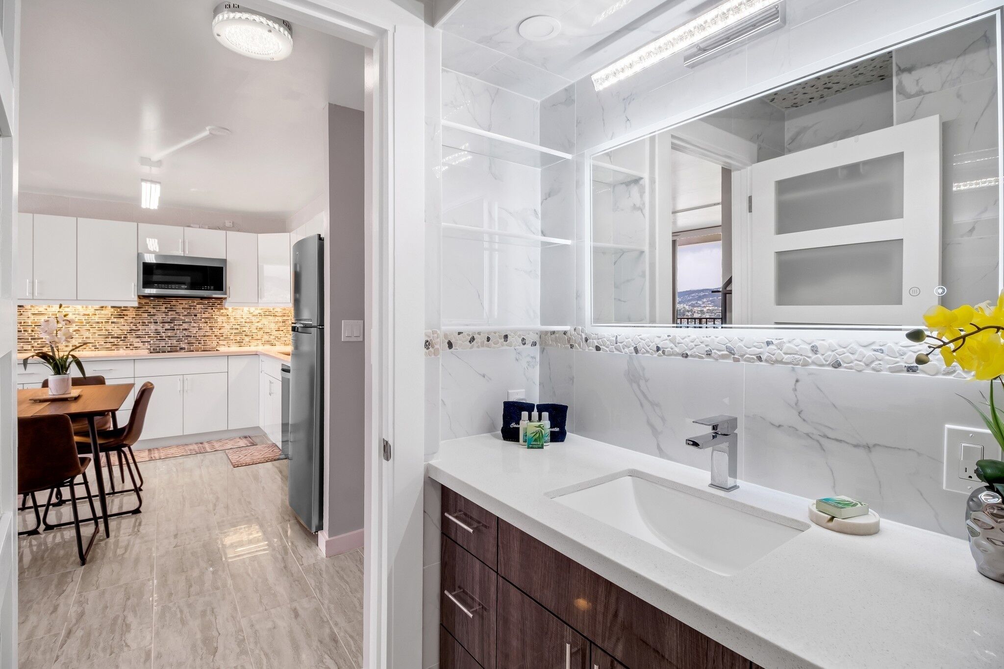 Cozinha moderna com armários brancos, painel de backsplash de tijolos e um espaço de refeições com mesa e cadeiras.