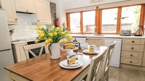 Cozinha com armários brancos, uma mesa de madeira e um vaso de flores amarelas. Há pratos com bolo e chá na mesa.