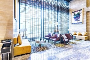 Um hall de hotel moderno com uma grande janela, um sofá, cadeiras e uma mesa de centro.