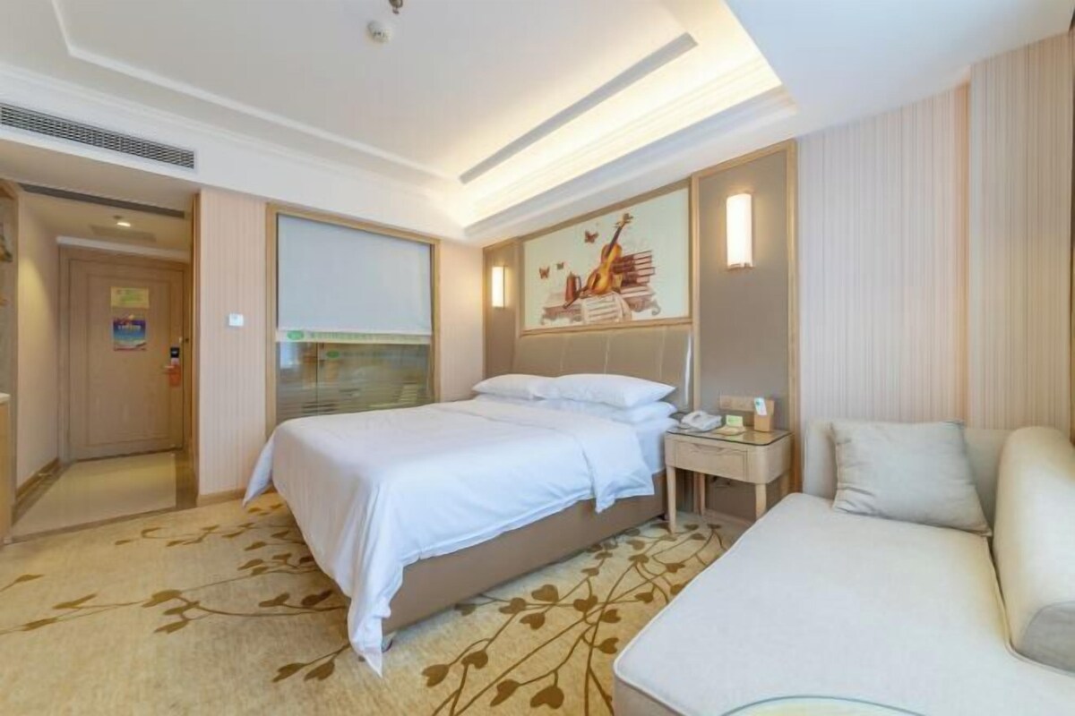 Quarto de hotel com cama grande, sofá, mesa de cabeceira e pintura na parede.