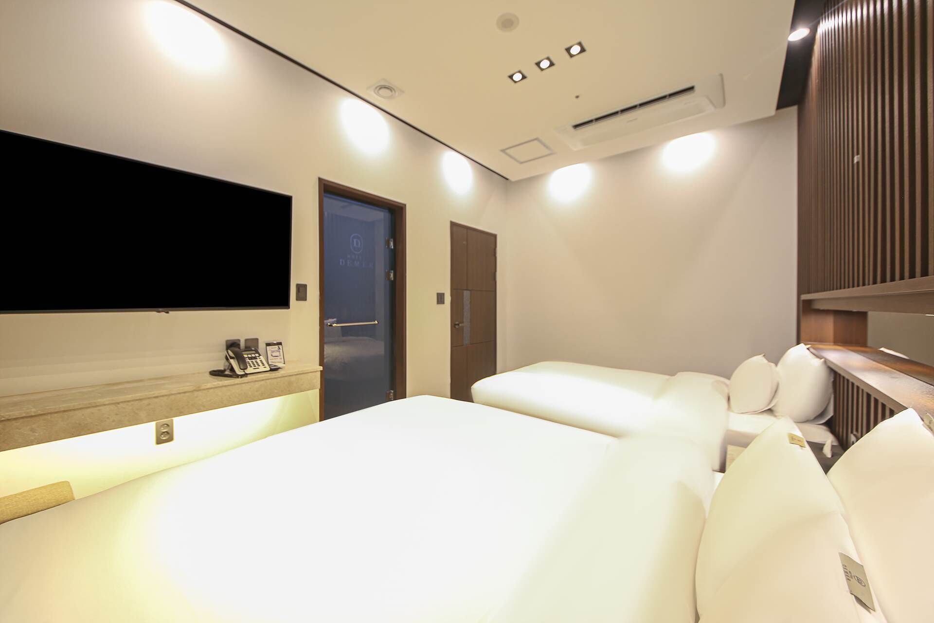 Quarto de hotel com uma cama grande, mesas de cabeceira, uma televisão e uma porta para o banheiro.