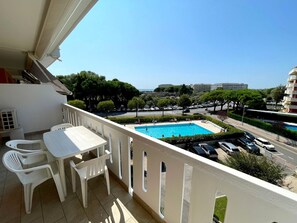 Uma varanda com vista para a piscina, cadeiras de plástico branco e uma mesa.